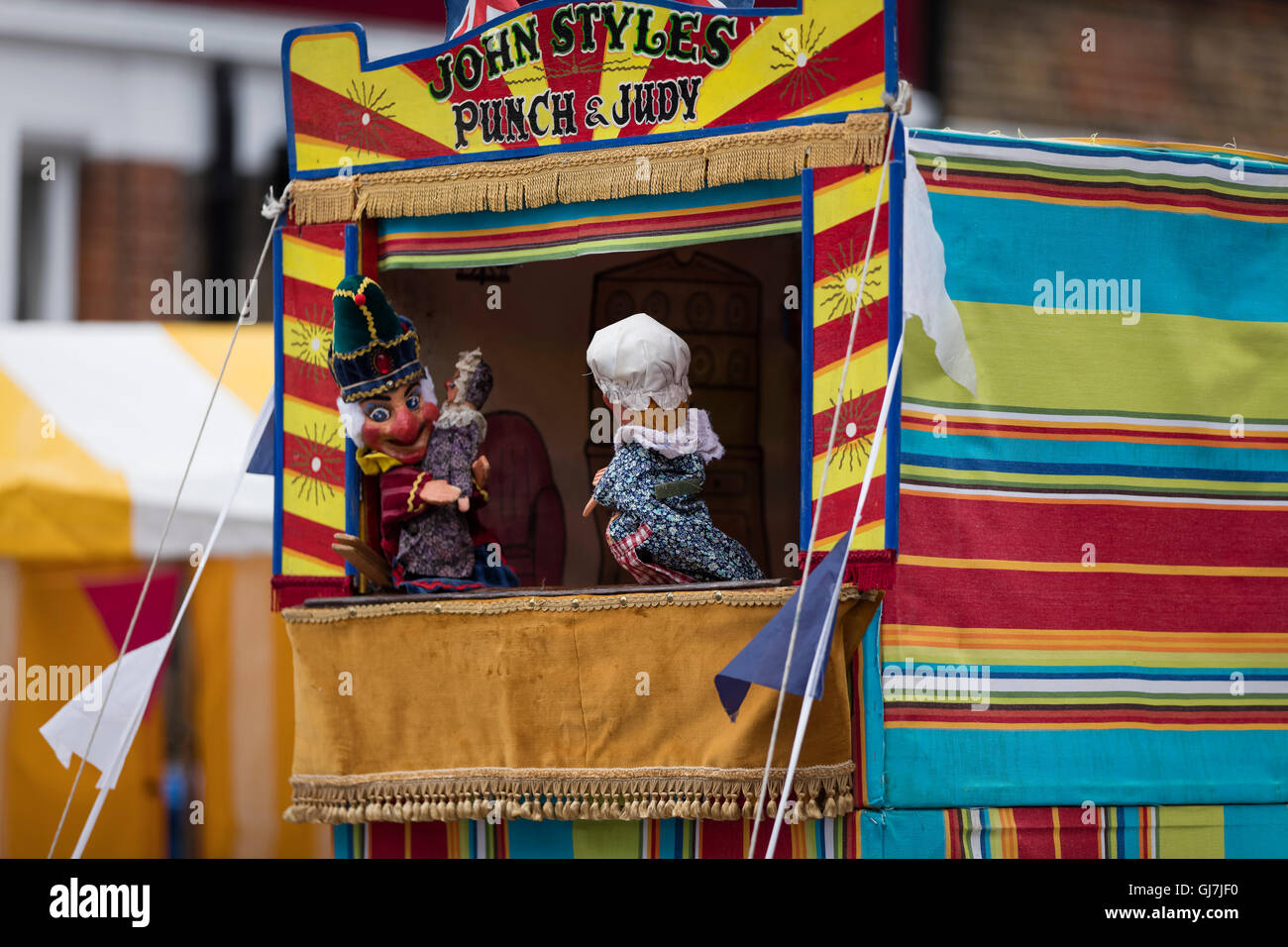 Mr Punch with Judy & baby in front of a Punch & Judy puppet booth. Unusual angle & limited depth ...