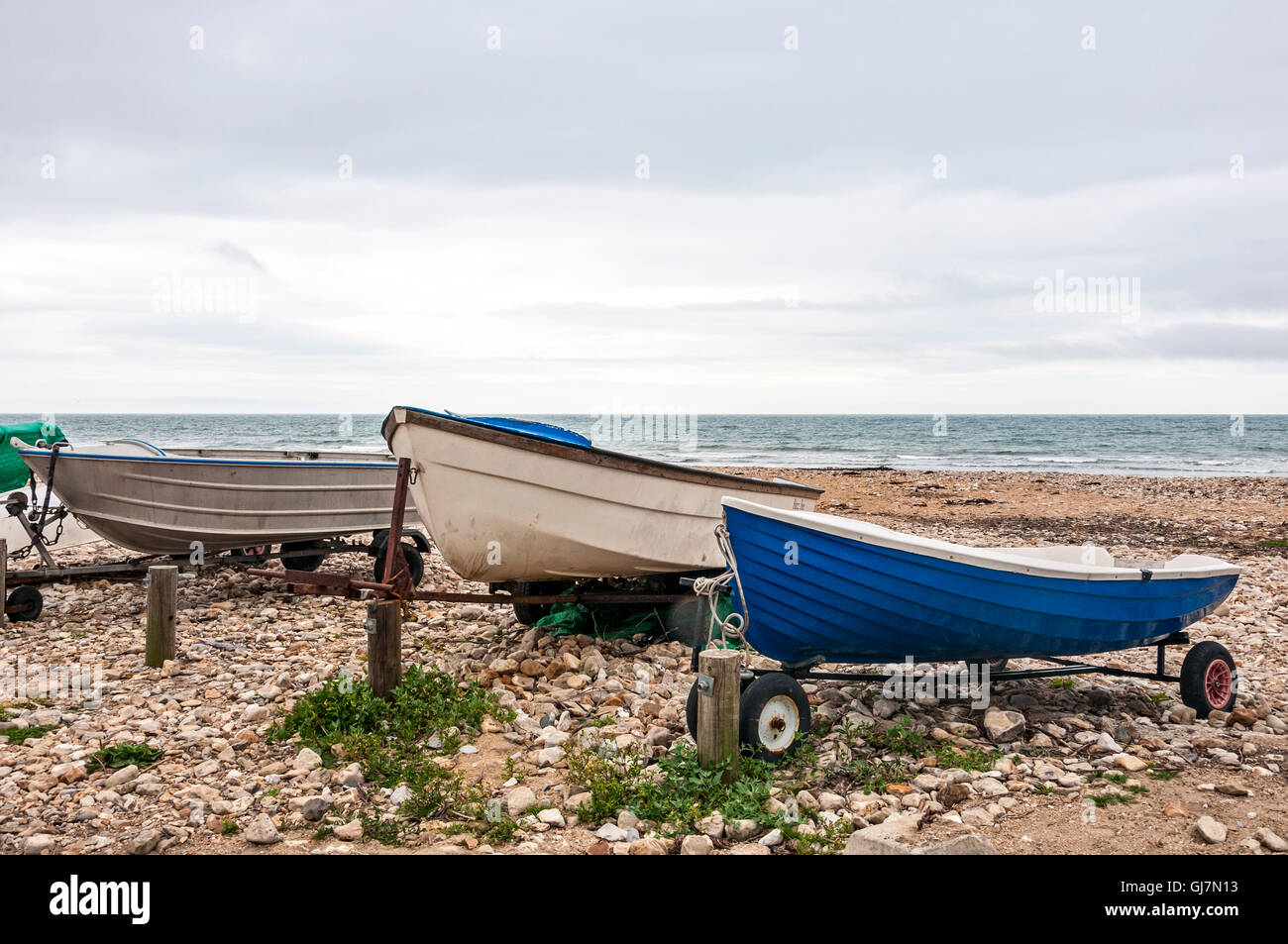 Three small boats rest on trailers moored to wooden stumps buried in a ...