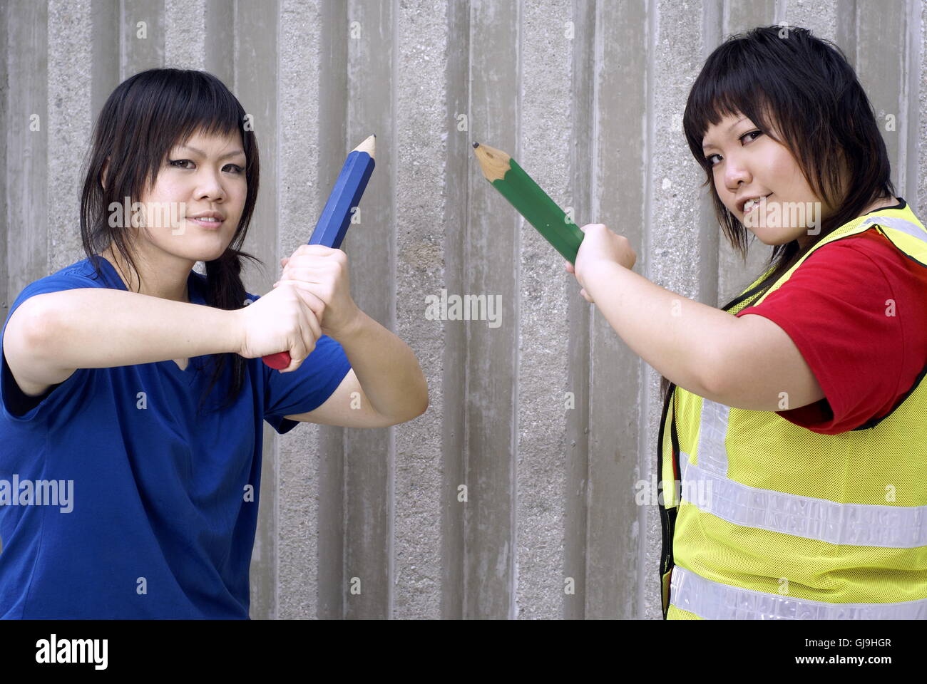 Two asian teen girls with large pencils in combative stance ...