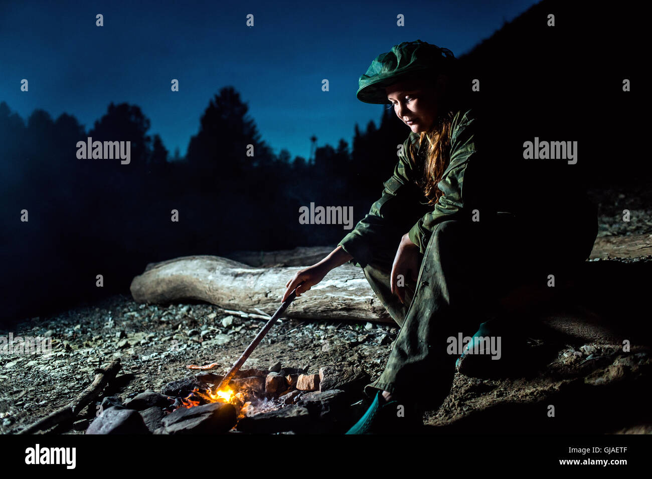 Girl stirs coals around the campfire Stock Photo - Alamy