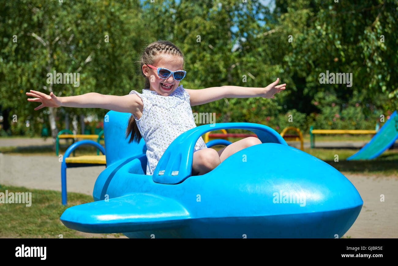 child girl fly on blue airplane attraction in city park, happy ...