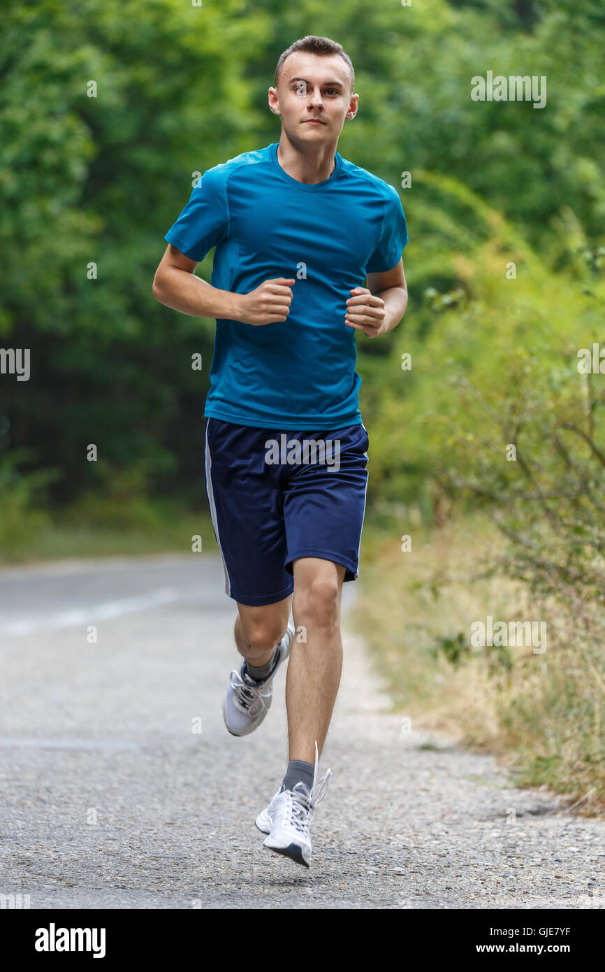 Young man running on a road through the forest Stock Photo - Alamy
