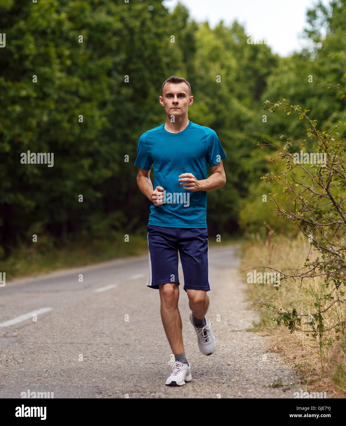 Young man running on a road through the forest Stock Photo - Alamy