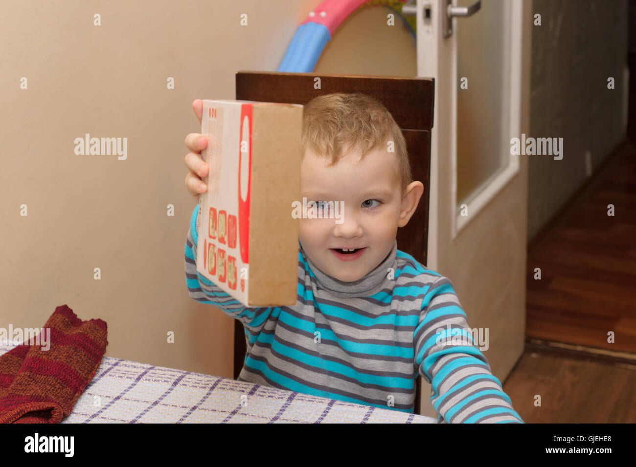boy sitting at a table with a cardboard box in which lies a wooden ...