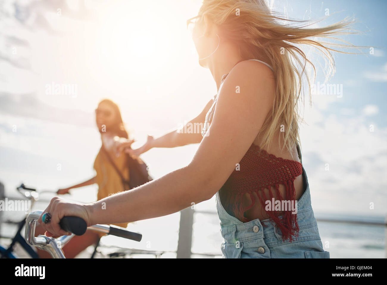 Two young female friends riding their bicycles on the seaside promenade ...