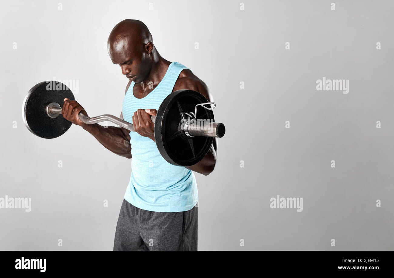 Shot of young african man working out with barbell against grey ...