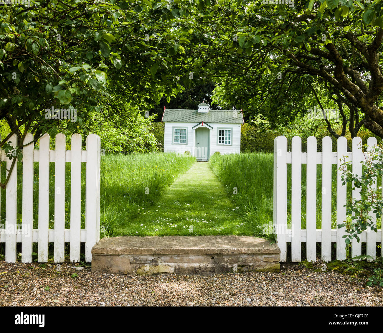A childs white playhouse at the end of a grass path, white picket fence ...