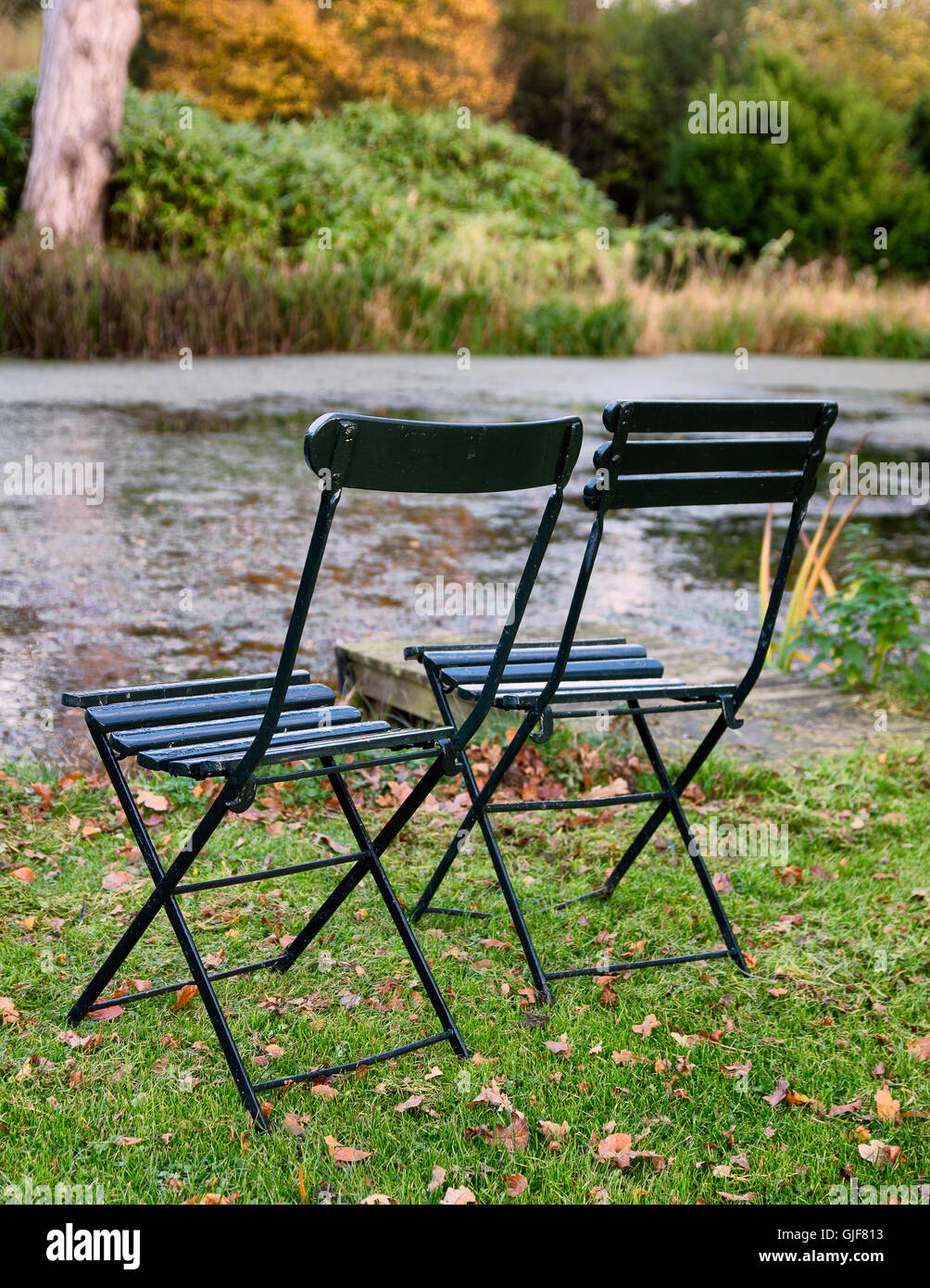 Two metal garden seats on the edge of a small lake Stock Photo - Alamy