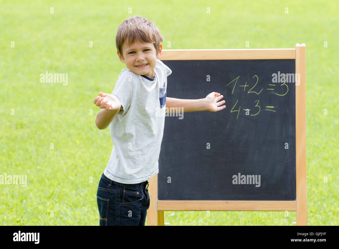 Boy thinking, writing and counting on blackboard. Green outdoor ...