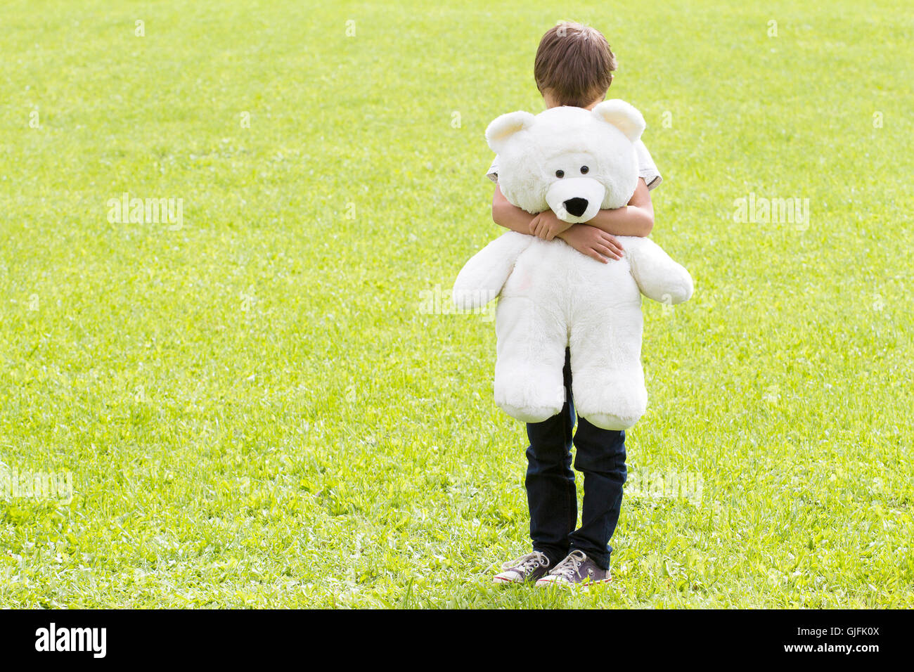 Disappointed boy is holding a teddy bear and standing on the meadow ...