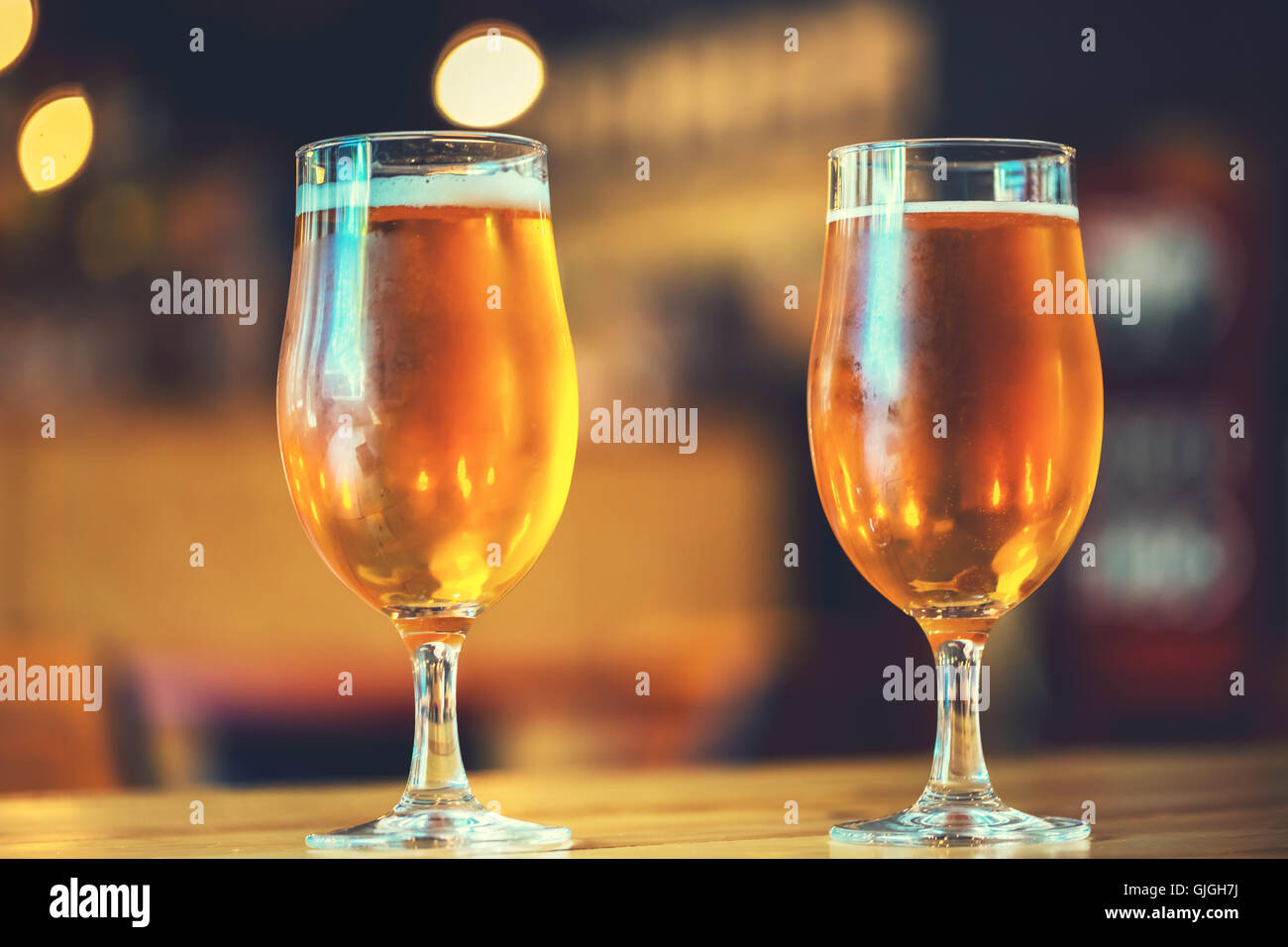 Two glasses of fresh cold light beer on a wooden bar counter in pub ...