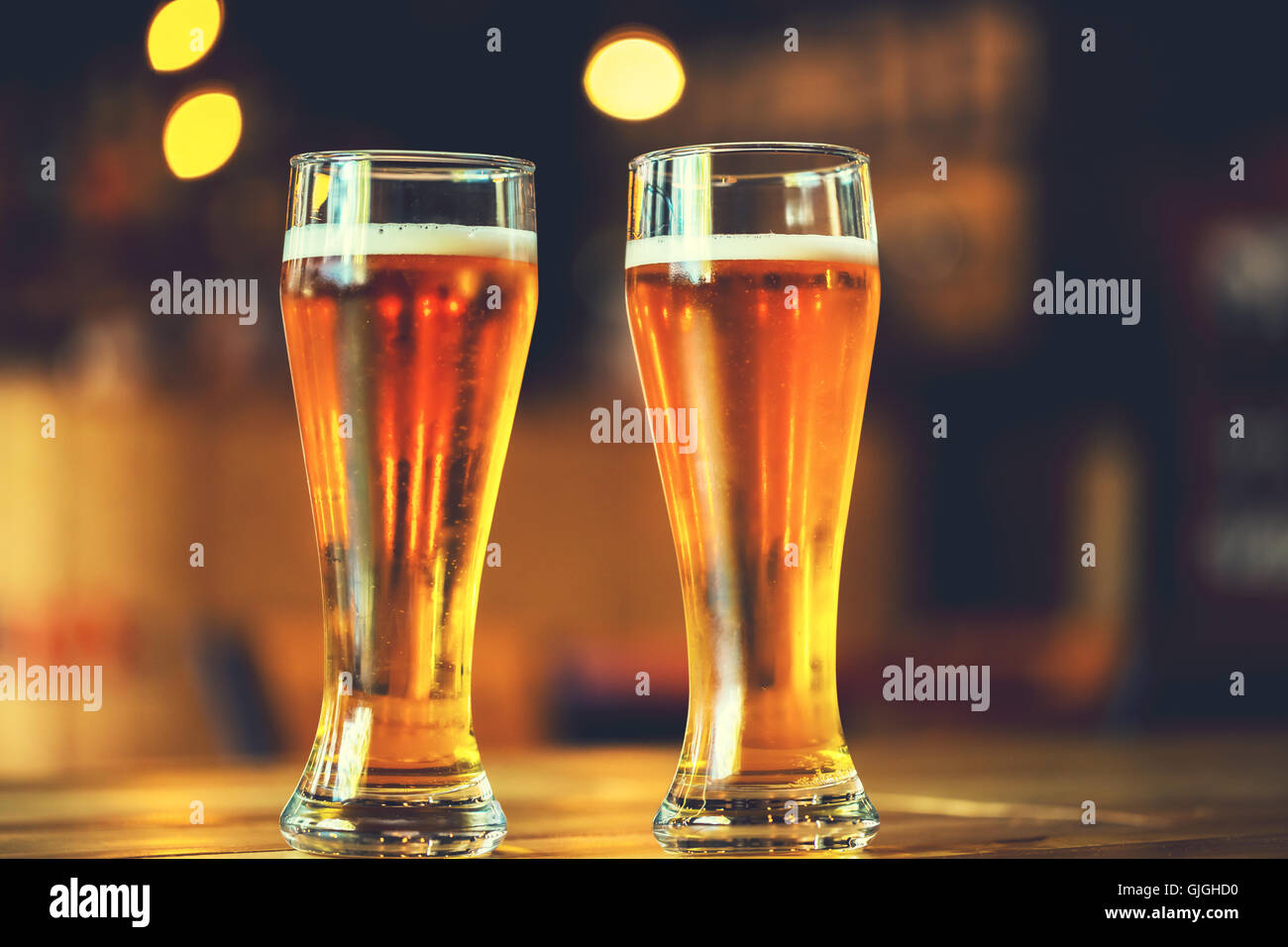 Two glasses of fresh cold light beer on a wooden bar counter in pub ...