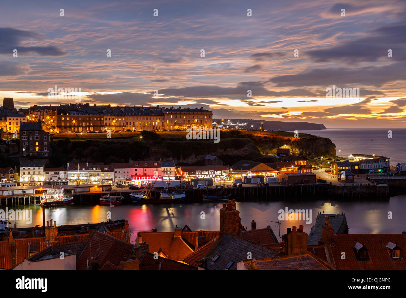 Whitby harbour and town, at night, with a dramatic sunset behind. In ...