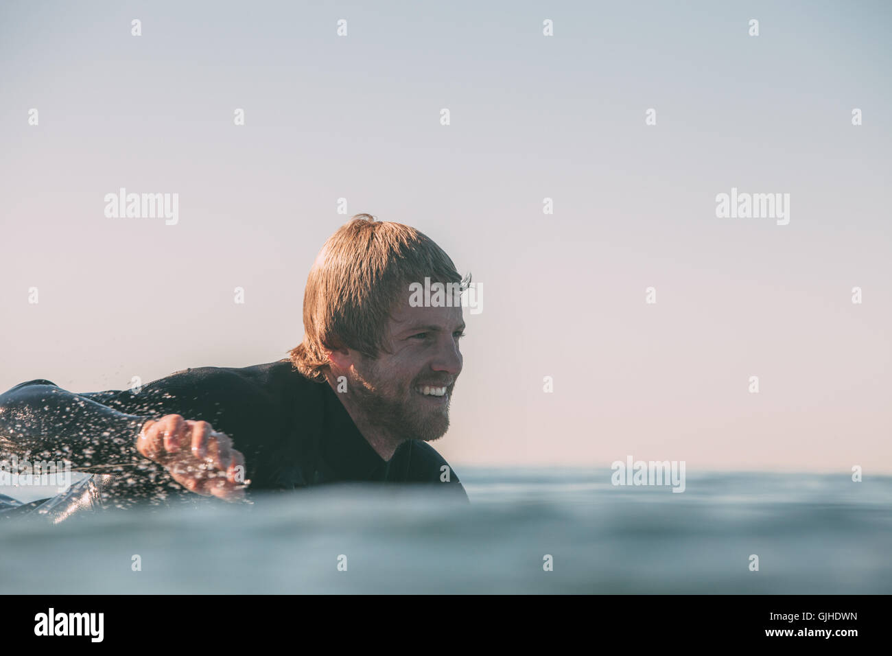 Close-up of a smiling surfer paddling out to catch a wave, San Diego ...