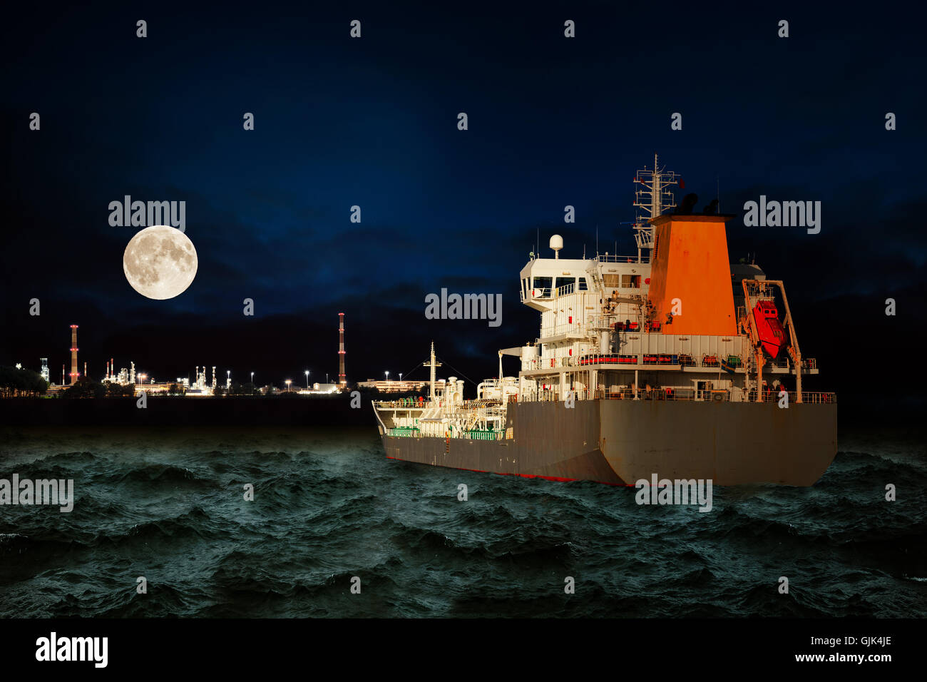 Tanker ship on sea with oil refinery industry in background at night ...