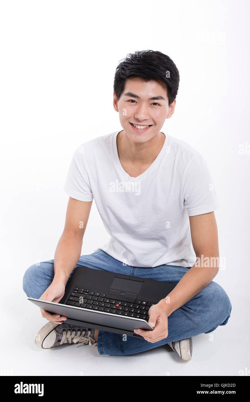 Studio shot of young casual man sitting cross-legged using laptop Stock ...