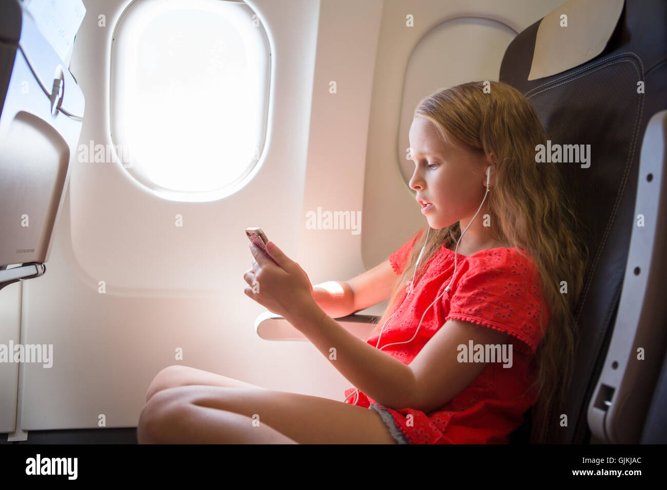 Adorable little girl traveling by an airplane. Kid listening music ...
