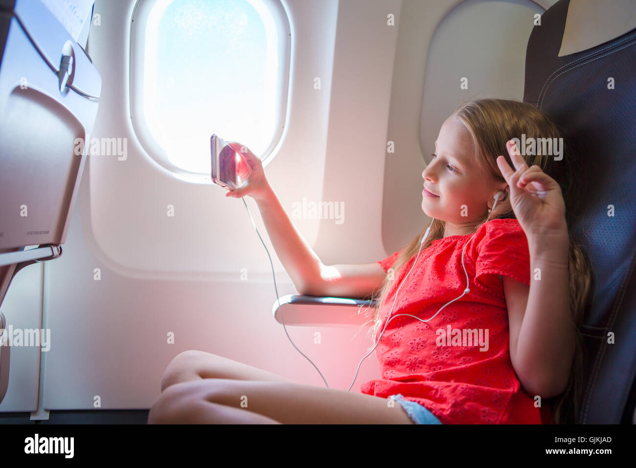 Adorable little girl traveling by an airplane. Kid listening music ...