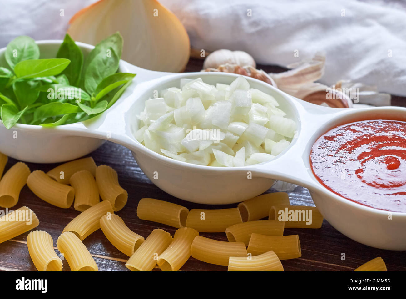 Basil, sliced onions and tomato paste in white bowl with raw pasta and ...