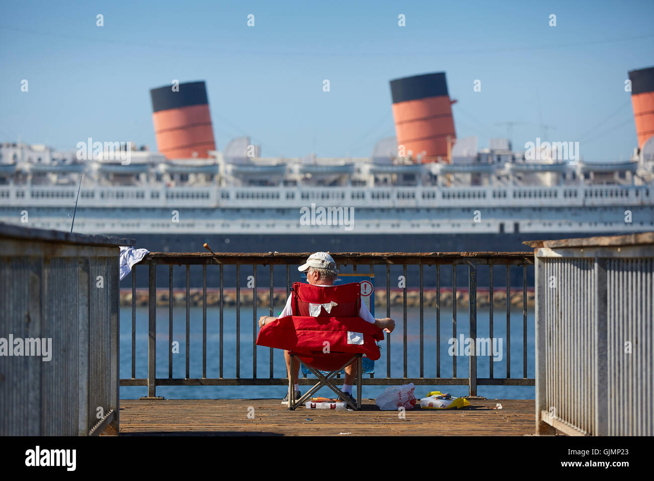 Man Sitting Fishing From A Pier Overlooking The RMS Queen Mary, Long ...