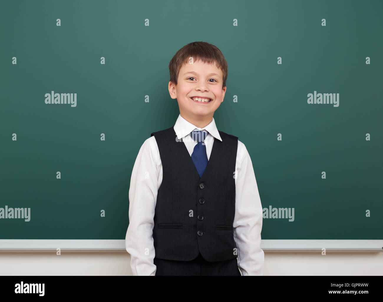 school student boy posing at the clean blackboard, grimacing and ...
