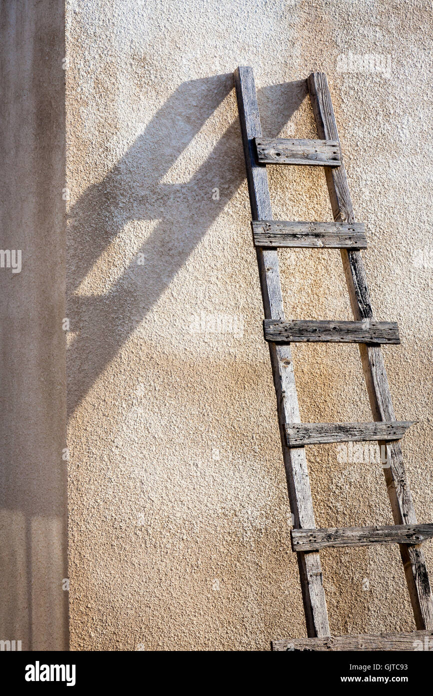 A ladder leans against a wall. The bright sunshine casts a strong ...