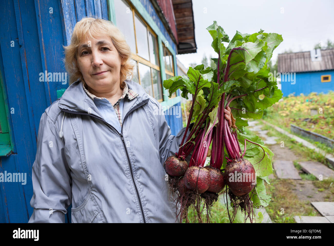 Smiling Caucasian woman holding fresh beet in hand while standing on ...
