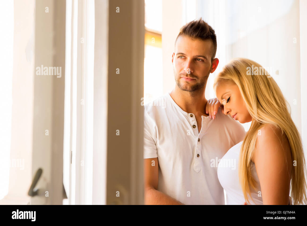 A beautiful young couple standing at the window at home Stock Photo - Alamy