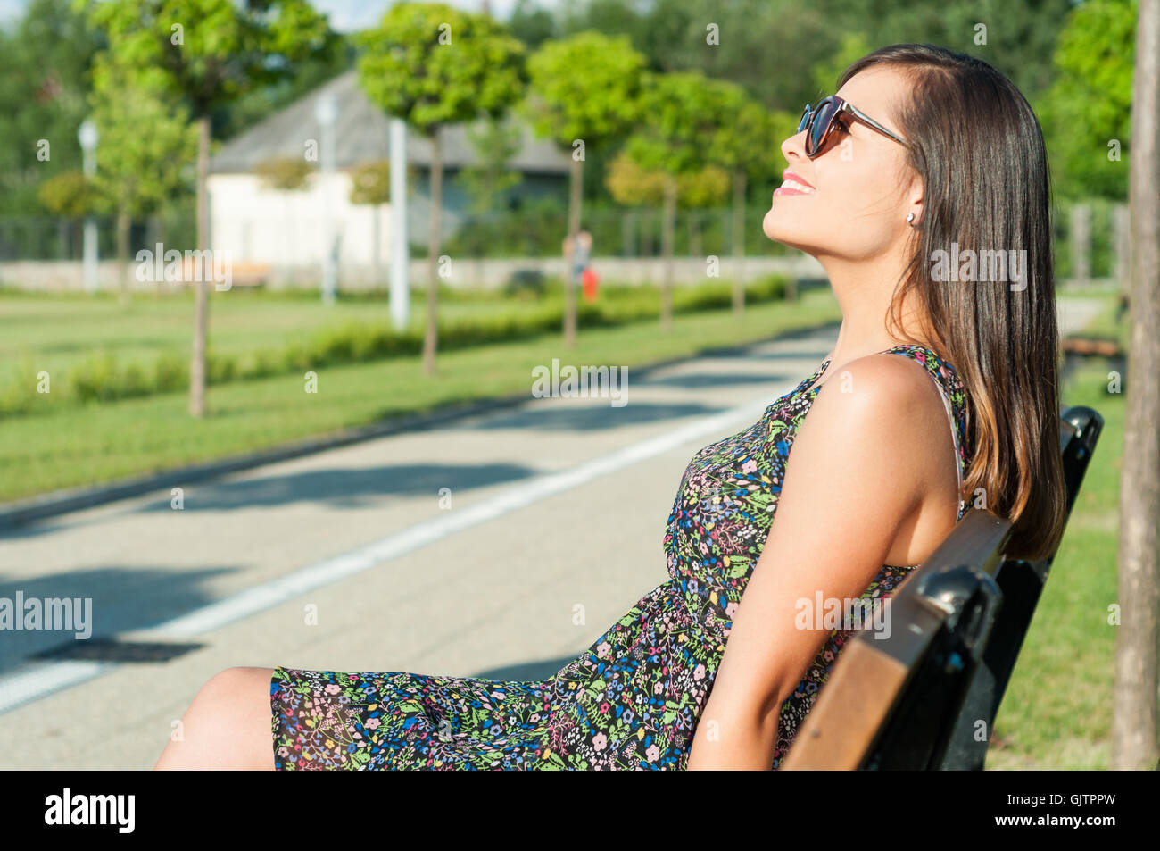 Pretty lady smiling enjoying sun outside in park sitting on a bench ...