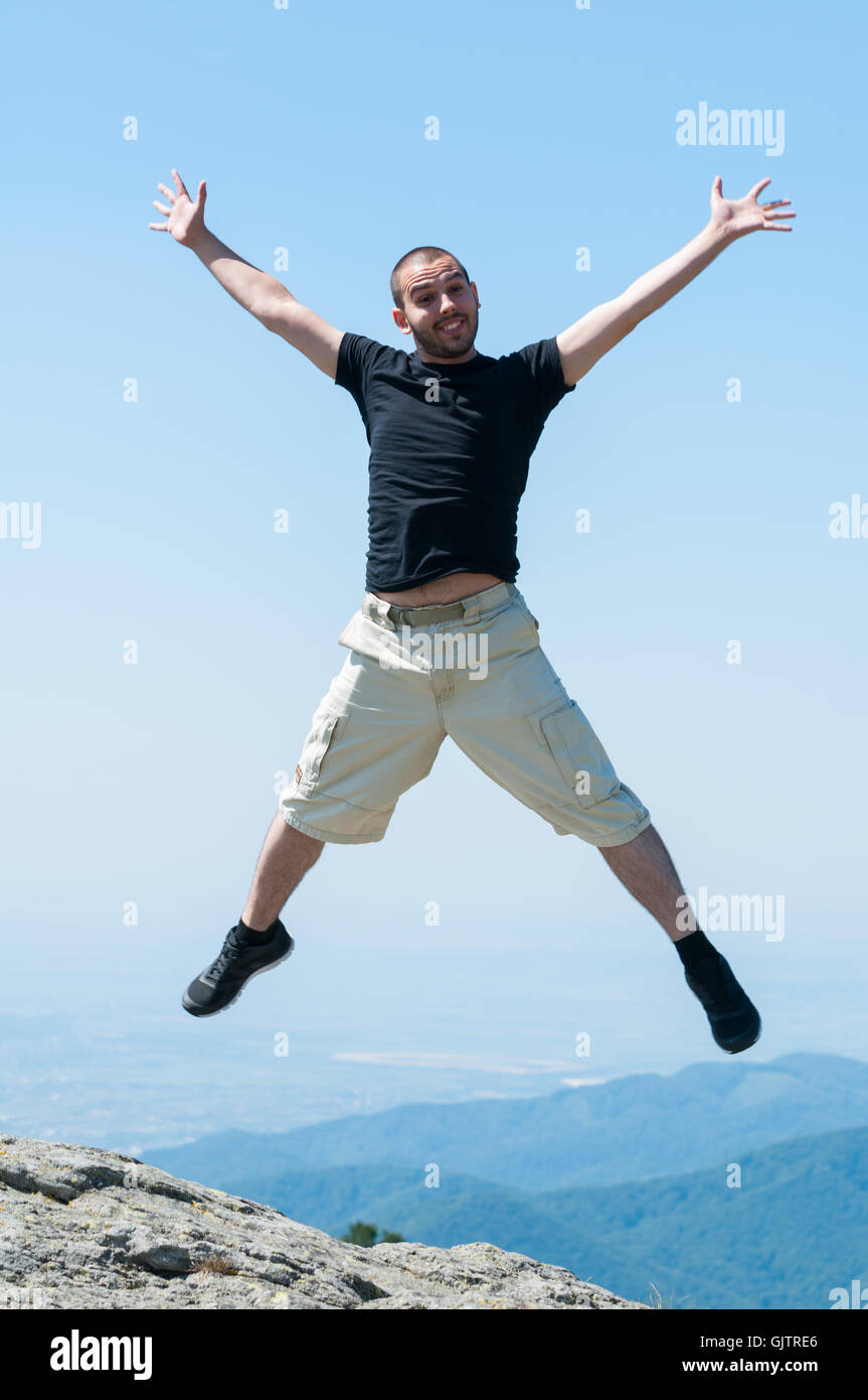 Happy cheerful man jumping on top of the mountain in a summer sunny day ...