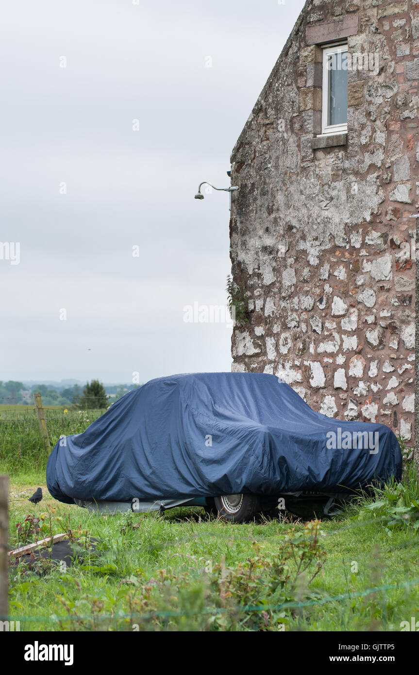 An old car stored outside in front of a stone building under a blue ...