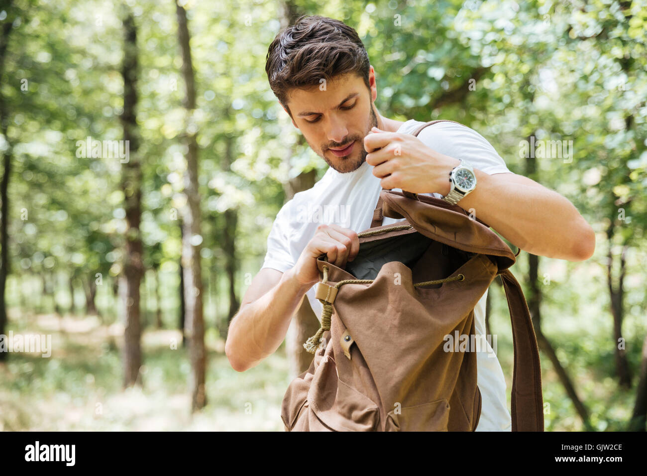 Handsome young man looking something in backpack in forest Stock Photo ...