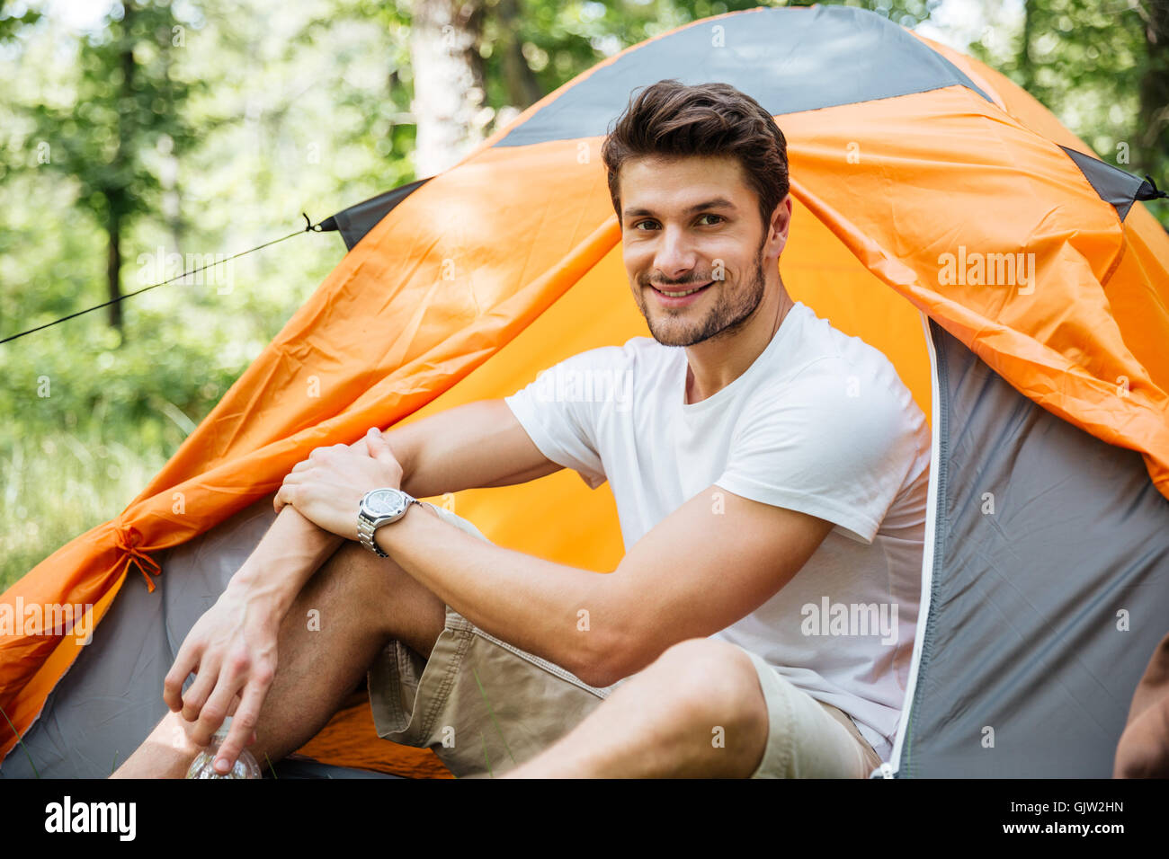 Cheerful young man tourist sitting in touristic tent in forest Stock ...