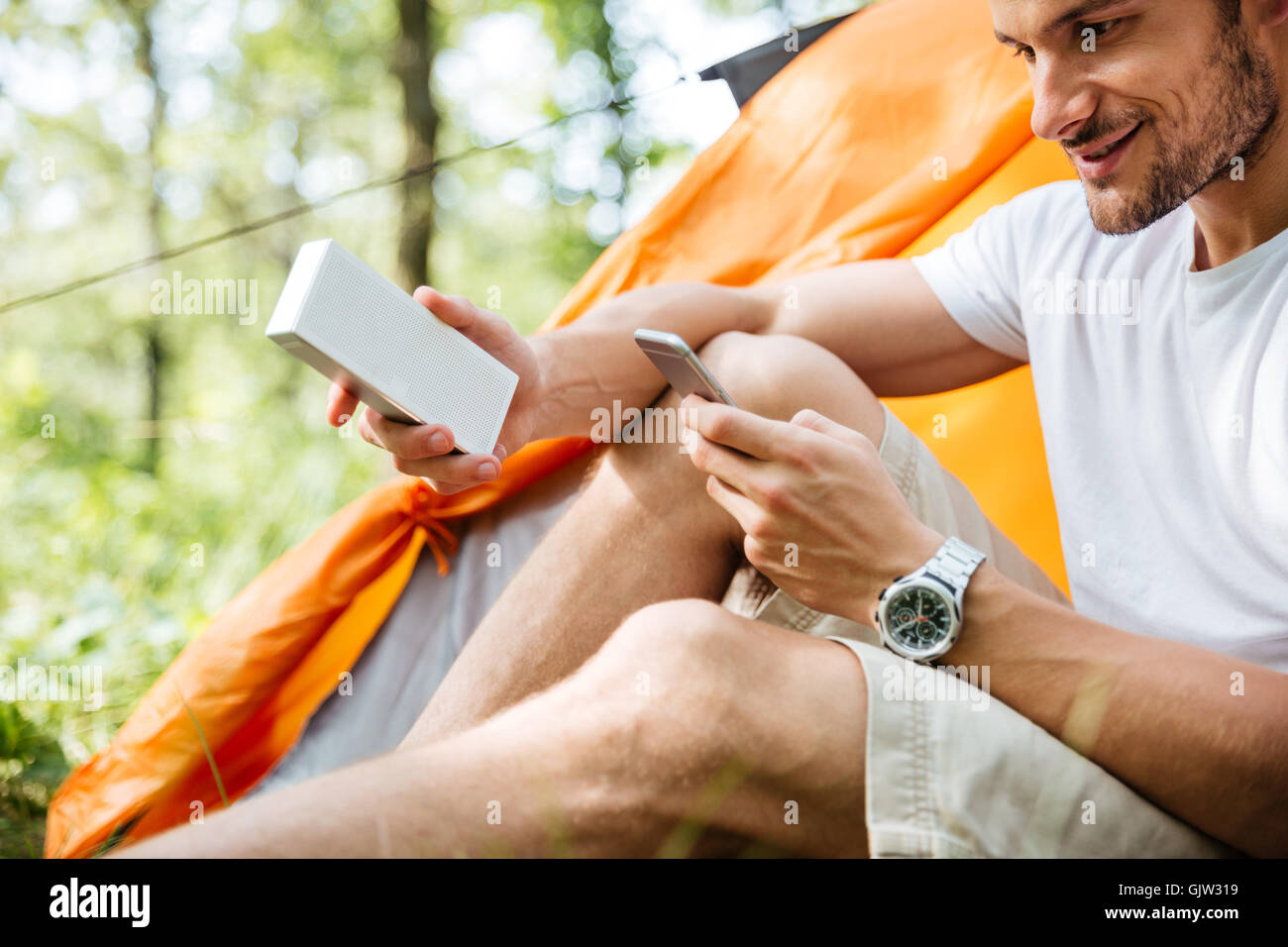 Smiling young man tourist using mobile phone and portable mini speaker ...
