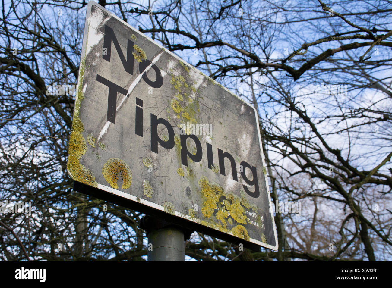 Very weathered and dirty No Tipping sign with blue sky and trees in ...