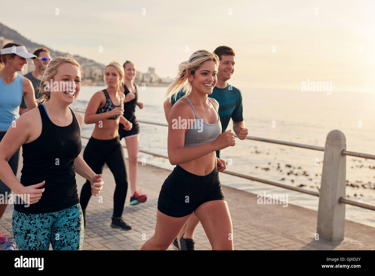 Young people running along a seaside promenade. Happy men and women ...