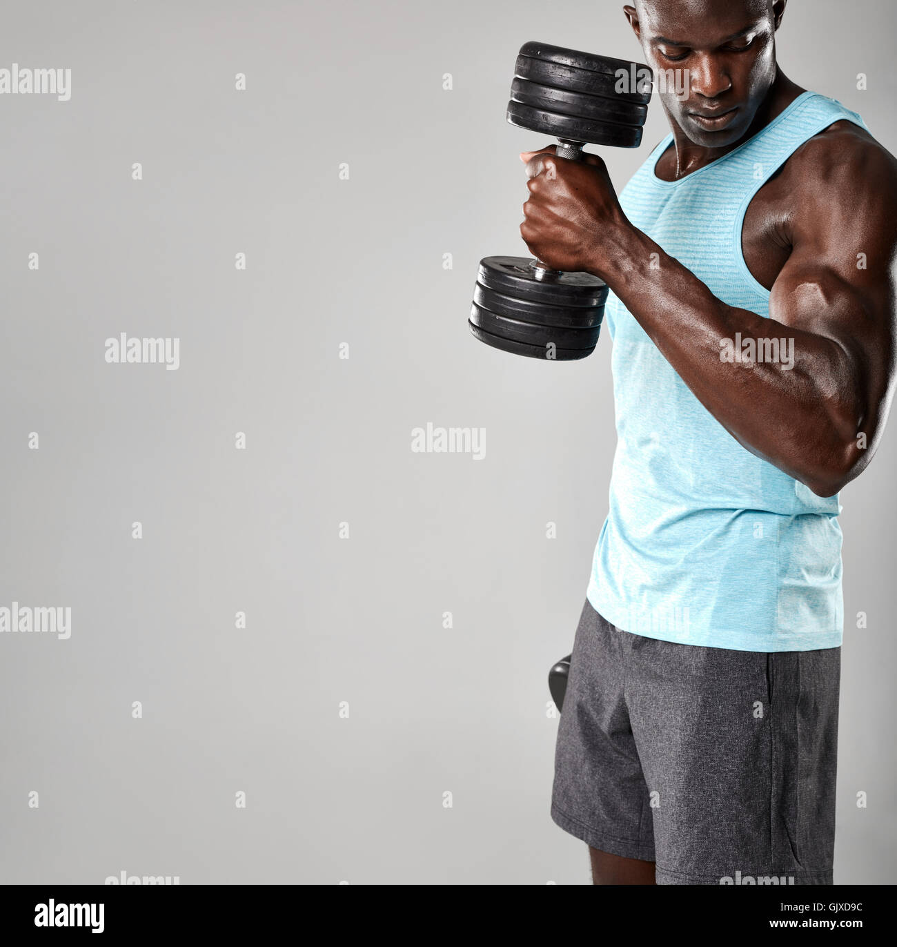 Shot of young african man working out with dumbbells against grey ...