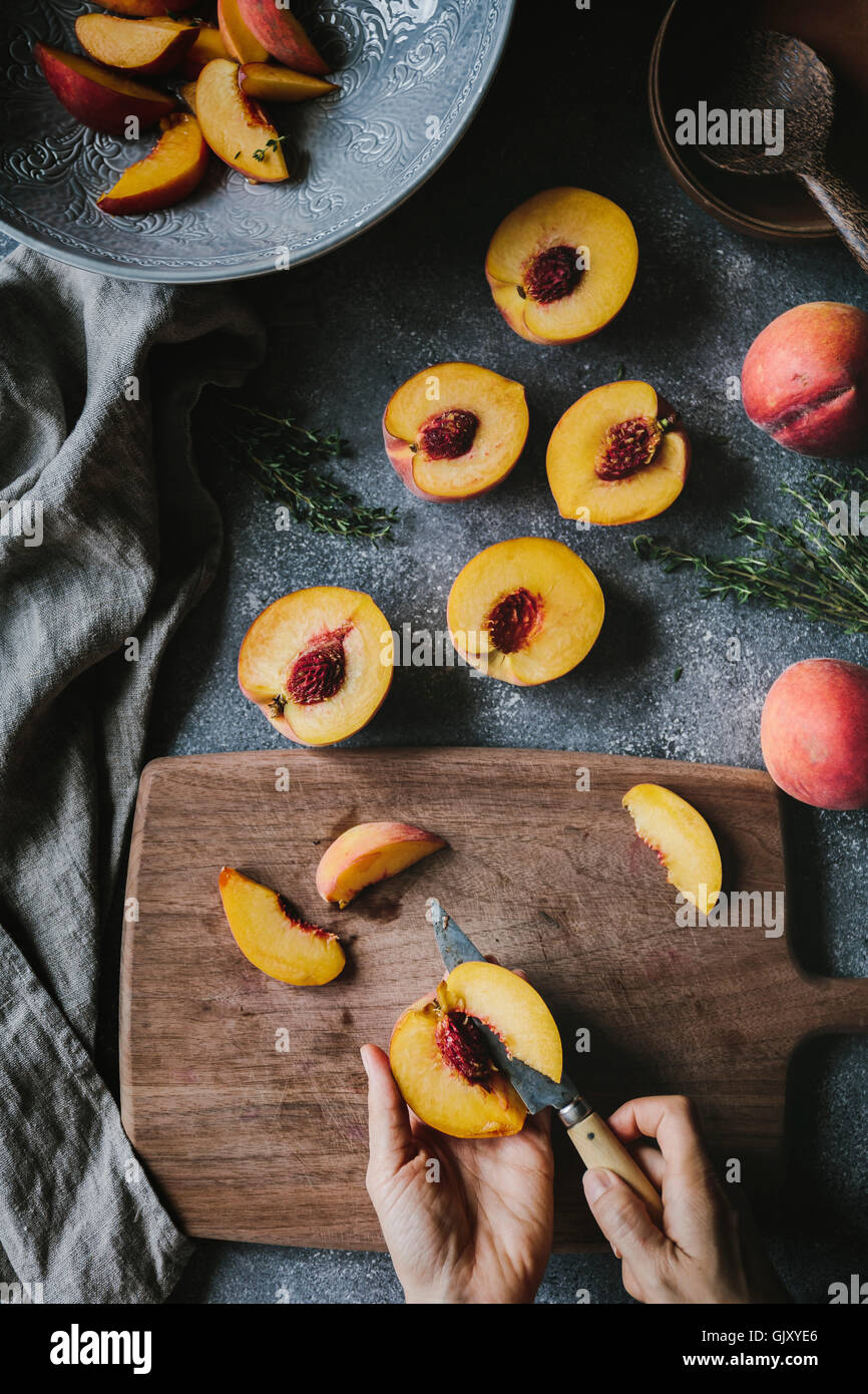 A woman's hands are photographed as she is slicing peaches from the top ...