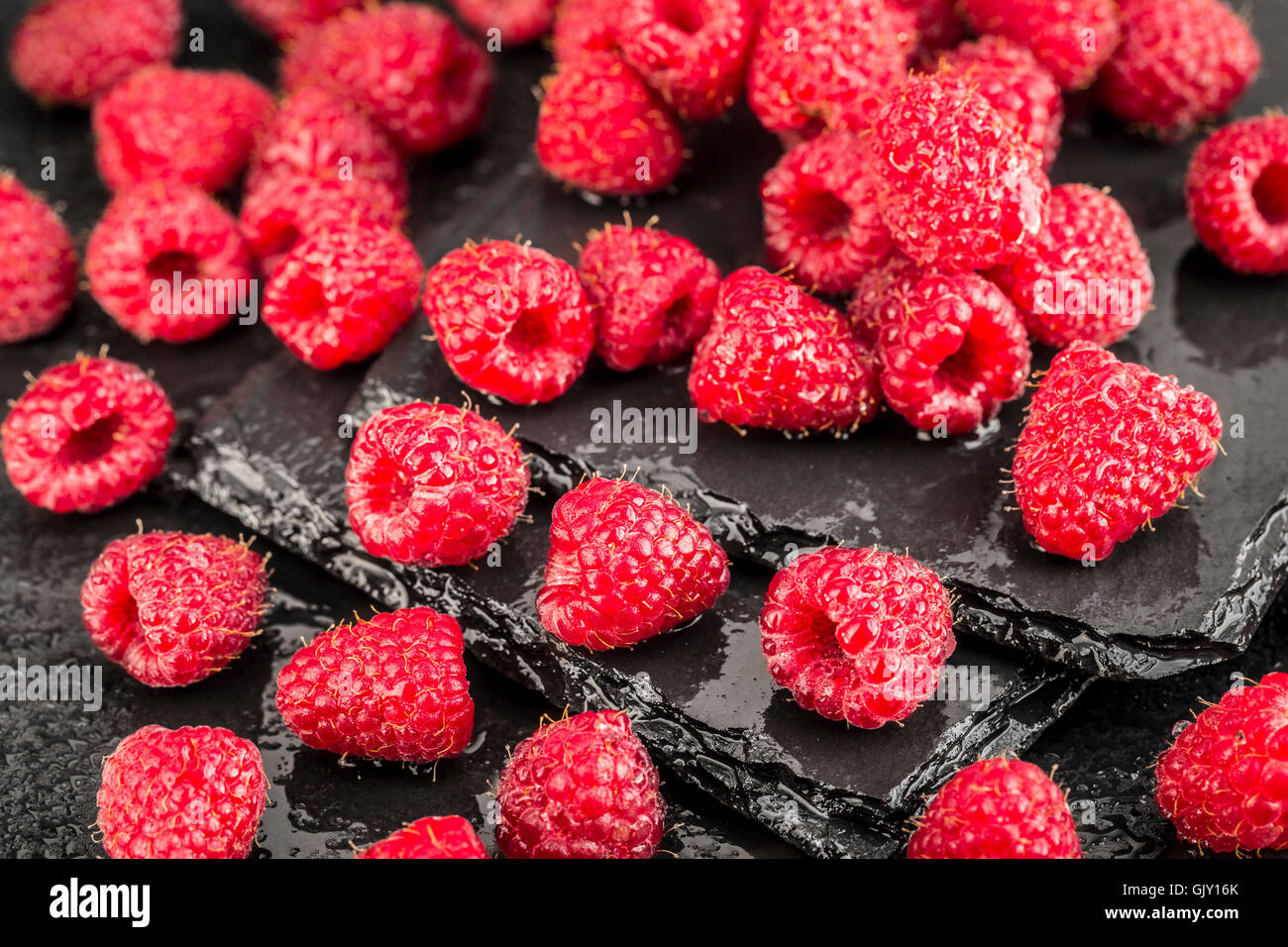 Wet red raspberries on a black slate background Stock Photo - Alamy