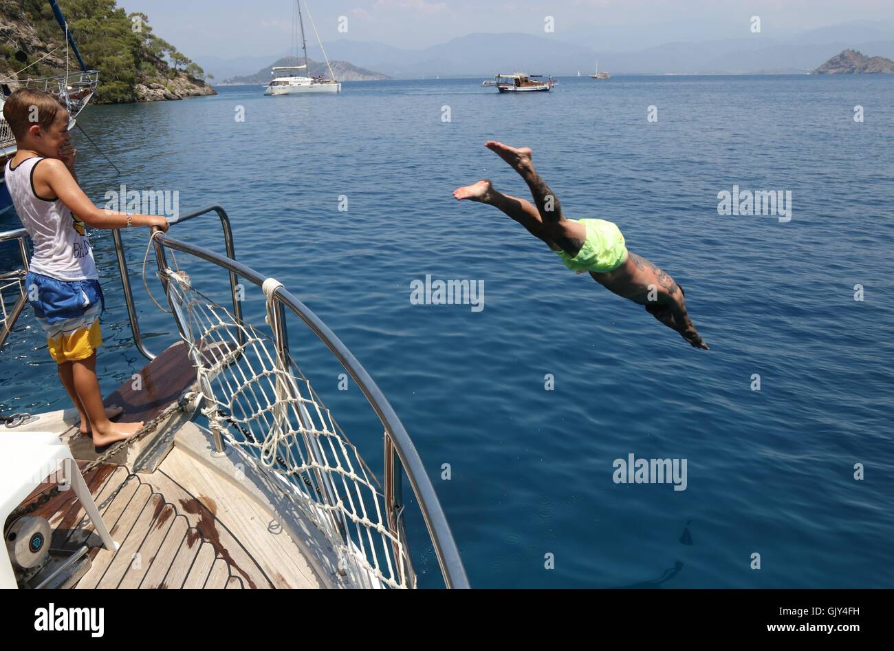 A man diving into the sea from the side of a boat being watched by his ...
