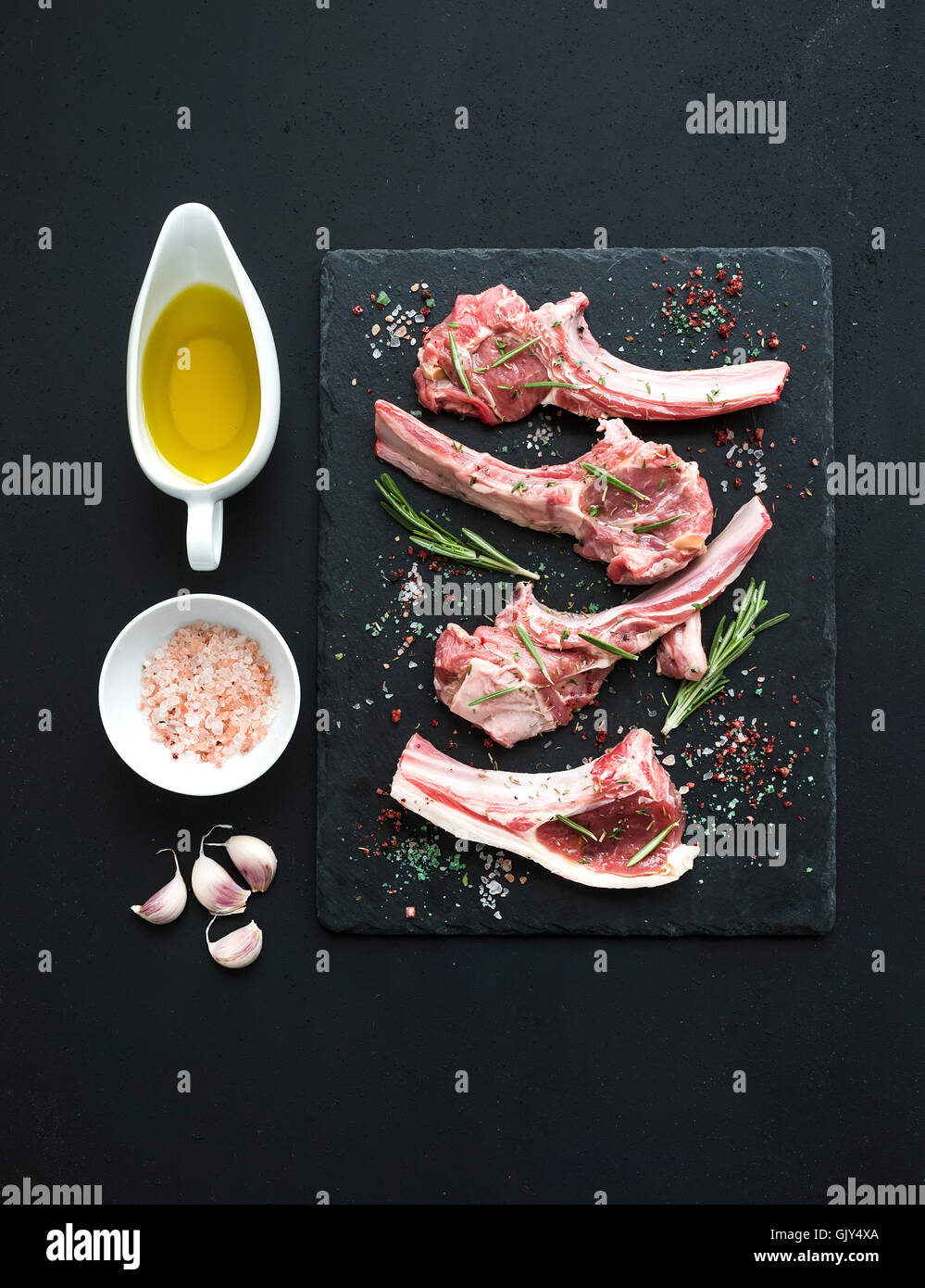 Raw uncooked lamb ribs with olive oil, spices and garlic on dark board ...