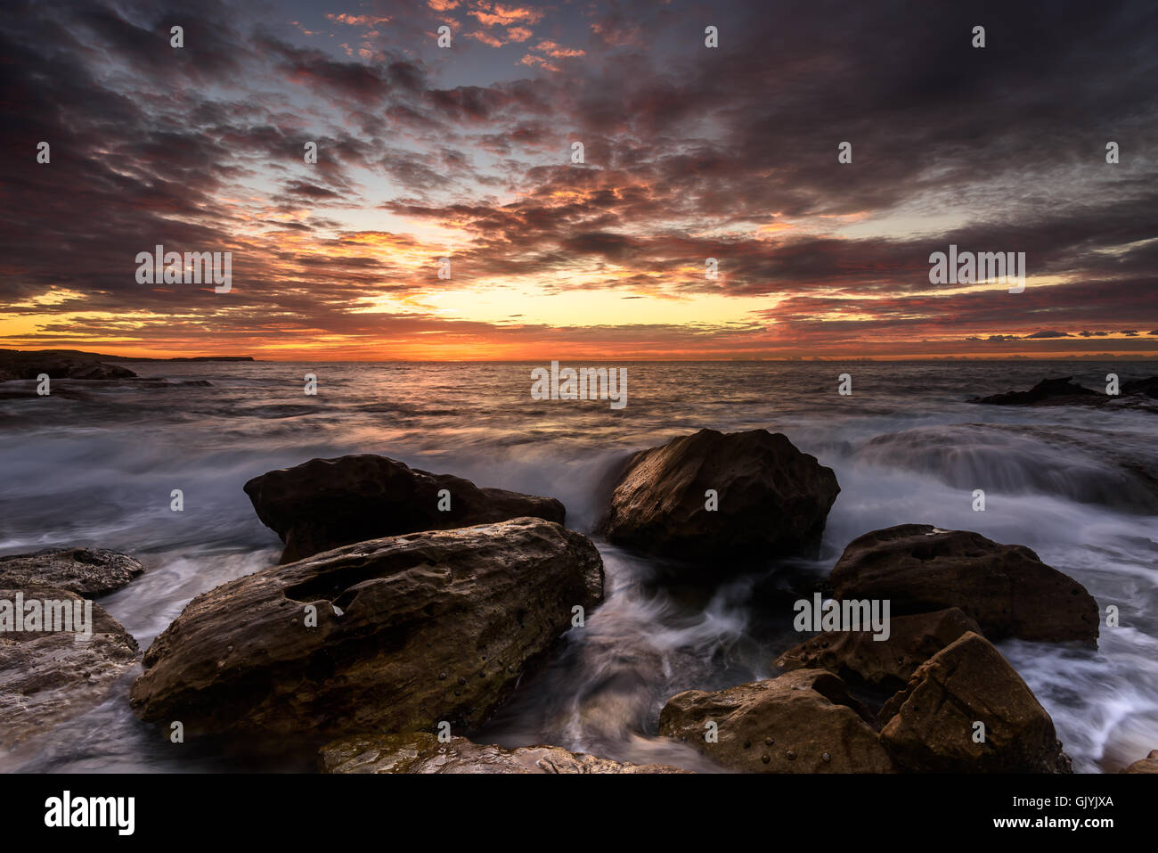 Sunrise over rocks by the ocean Stock Photo - Alamy