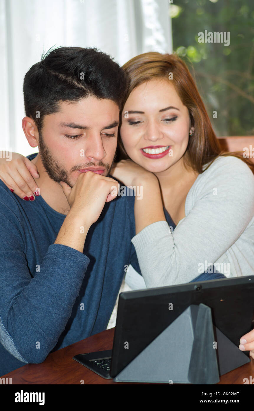 Young charming couple seated by table watching tablet screen while ...