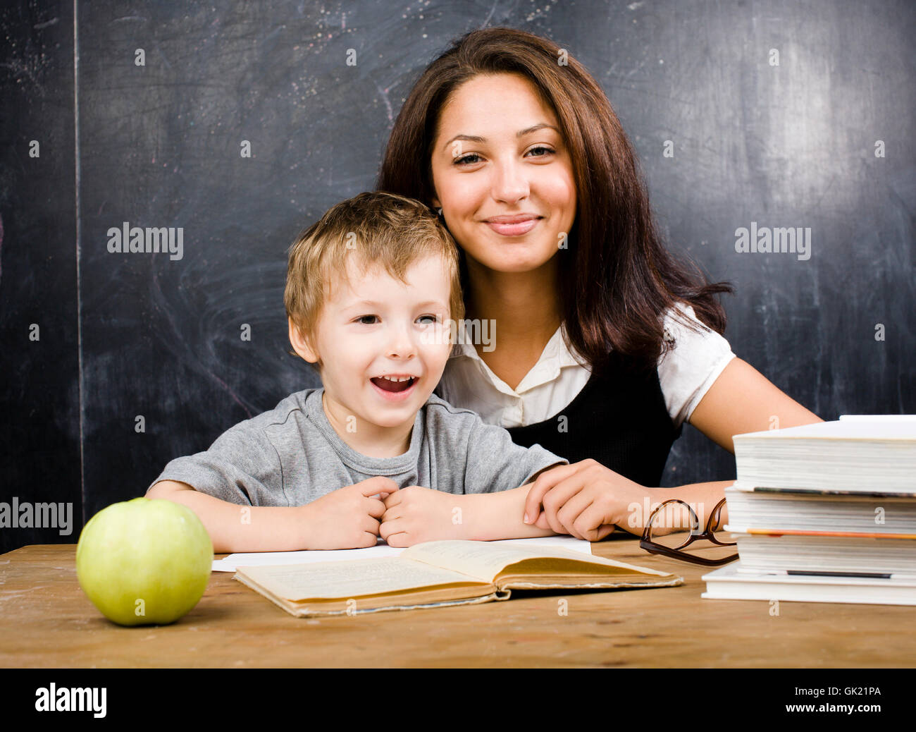 little cute boy with young teacher in classroom studying at blackboard ...