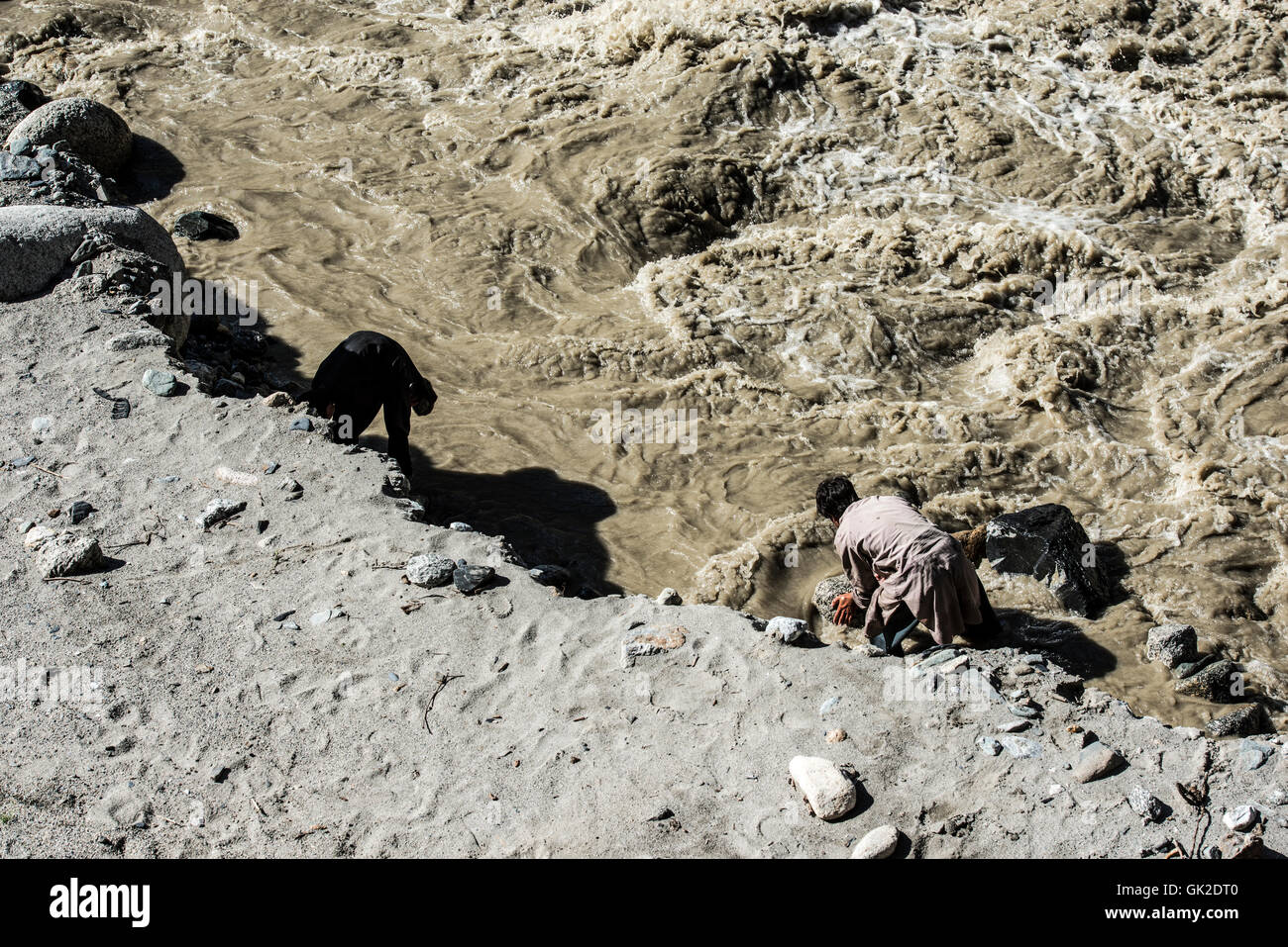 Two men working in a snow melt torrent (Kalash river). They are placing ...