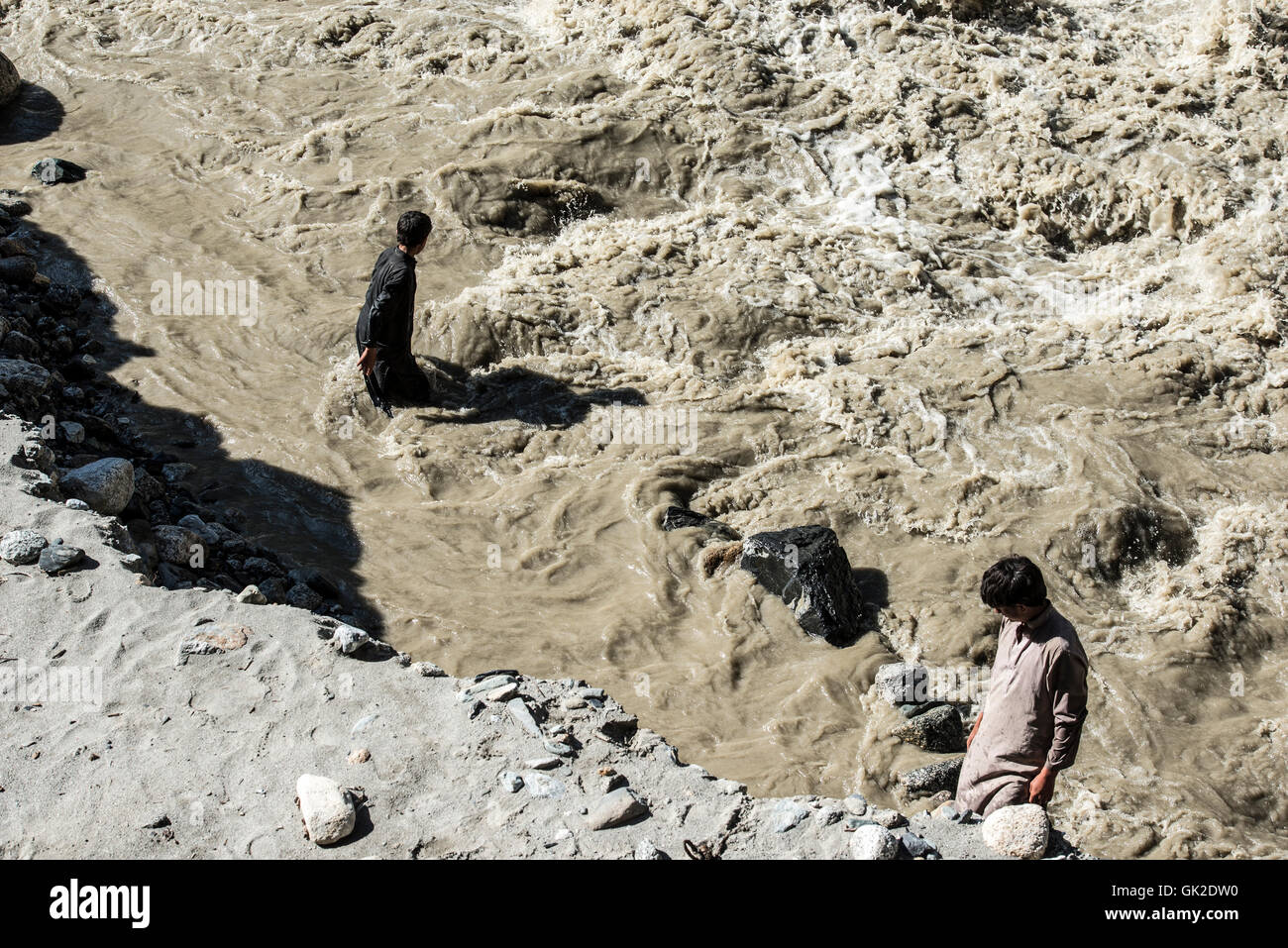 Two men working in a snow melt torrent (Kalash river). They are placing ...