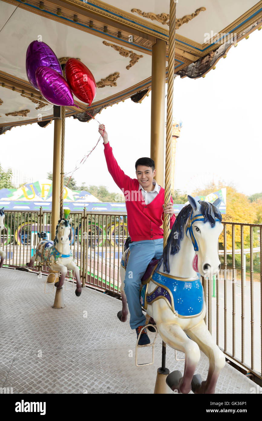 Young man in an amusement park ride carousel Stock Photo - Alamy