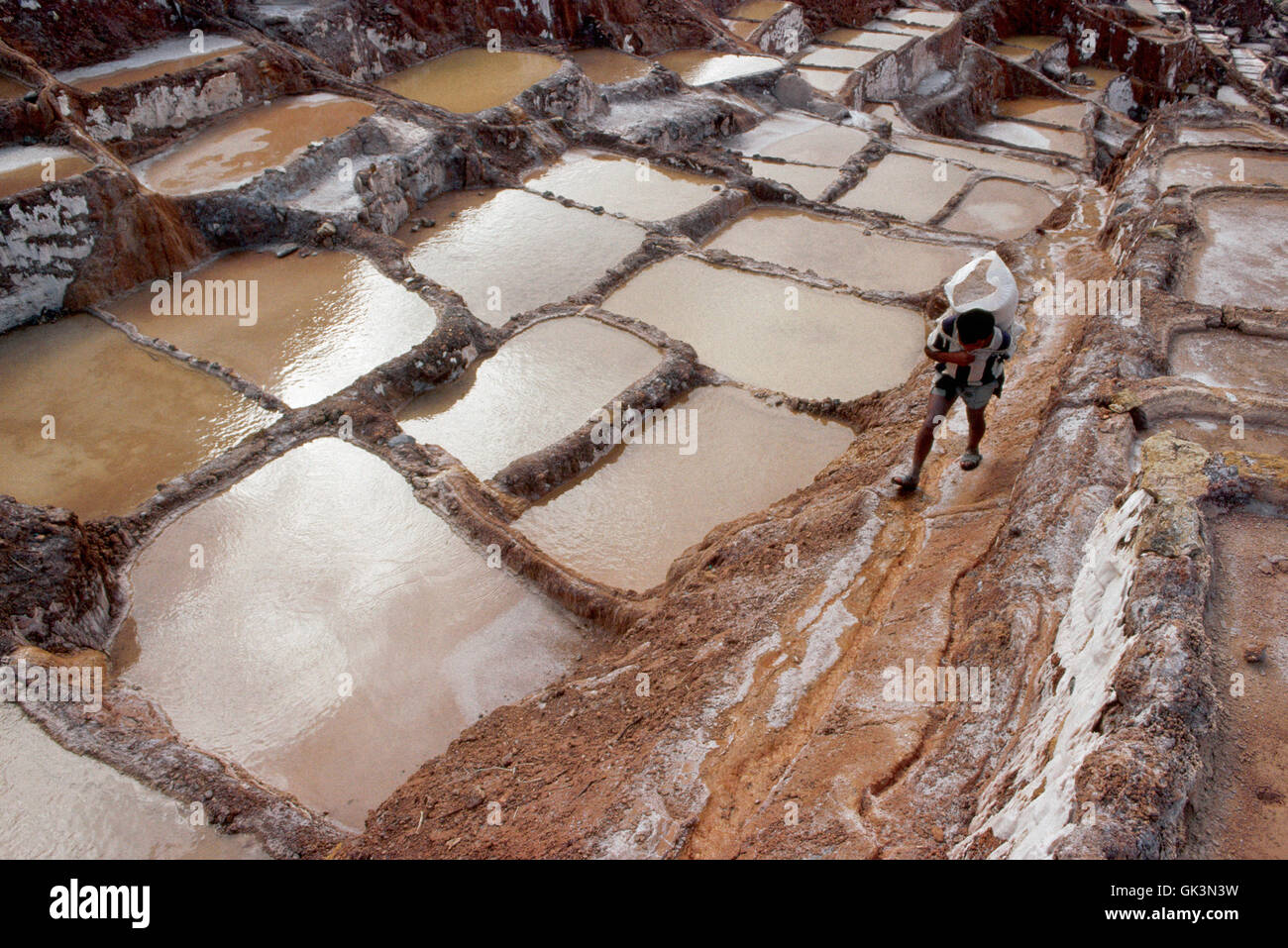 ca. 1980-1995, Maras, Peru --- Sacks of salt are carried along the ...