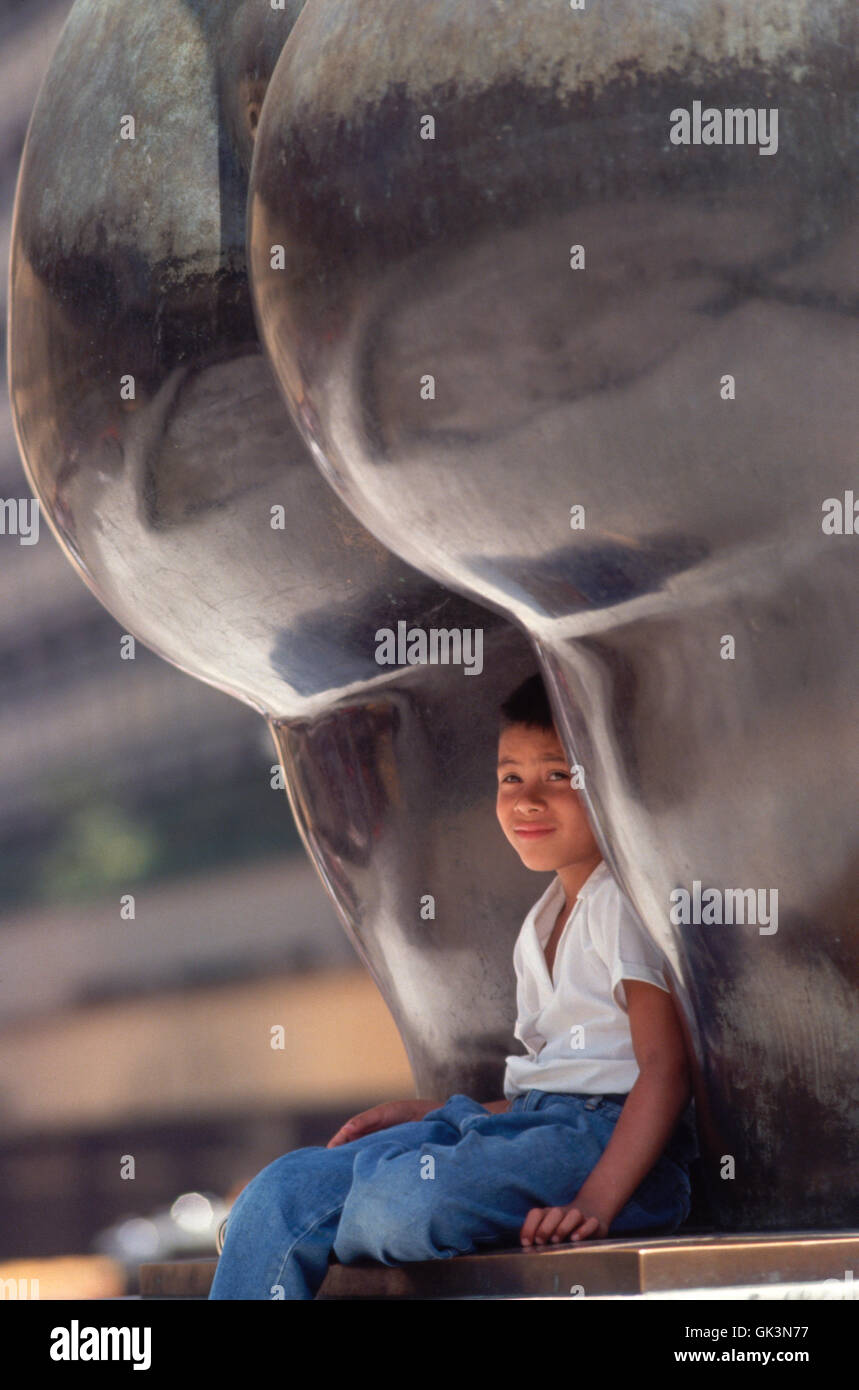 ca. 1980-1995, Medellin, Colombia --- A young boy sits against the El ...
