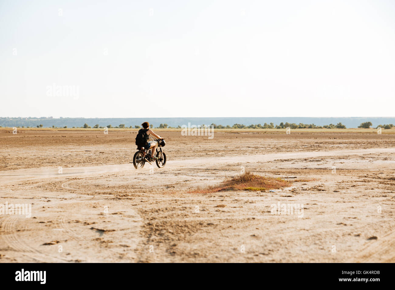 Man is kicking up dust as he rides his motorcycle through the desert ...